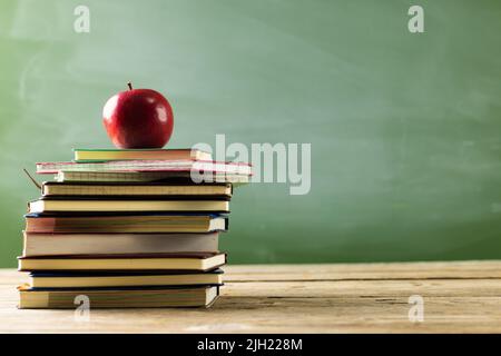 Image of books, notebook and apple on wooden table over black board ...