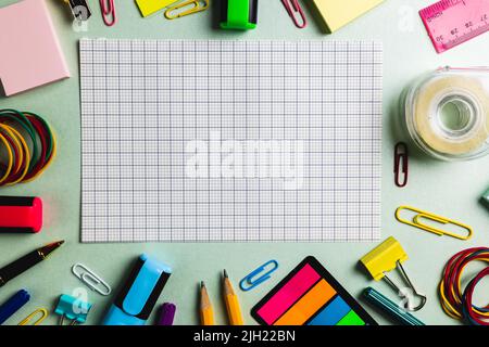Composition of checked sheet and frame made of school tools on green ...