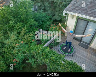 senior man is exercising on a mini trampoline in his backyard patio ...