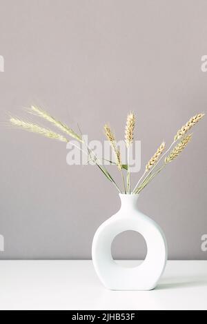 Stylish circle vase with dried spikelets bouquet on light table, copy ...