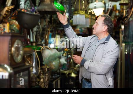 Male is visiting the market of old things and choosing lamp outdoors ...