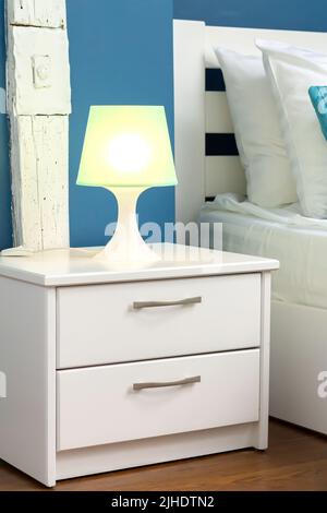 A minimalist bedside table with drawers and a light hanging over it ...