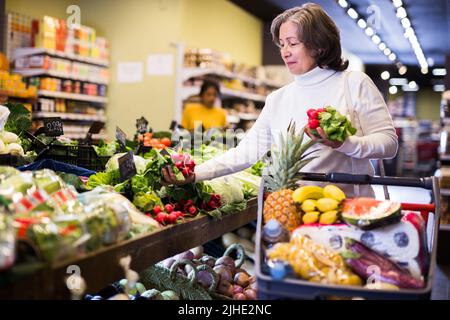 Mature woman picks ripe radishes on shelves in grocery shop Stock Photo ...