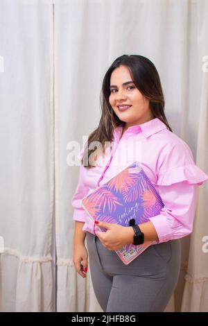 A plump young woman in pink shirt and glasses holding a notebook and ...
