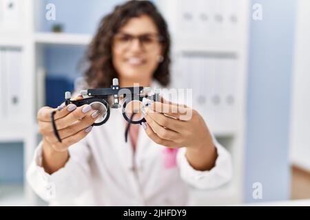 Young latin woman wearing optician uniform holding optometrist glasses ...