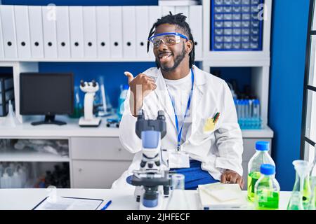 African man with dreadlocks working at scientist laboratory with hand on head, headache because ...