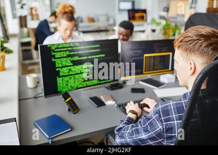 Young IT specialist writing codes for program on computer while sitting ...