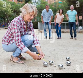 Cheerful males and females playing petanque in th park on holidays ...
