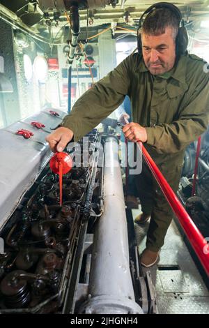 Man, engineer, oiling a large diesel engine in the engine room of the ...