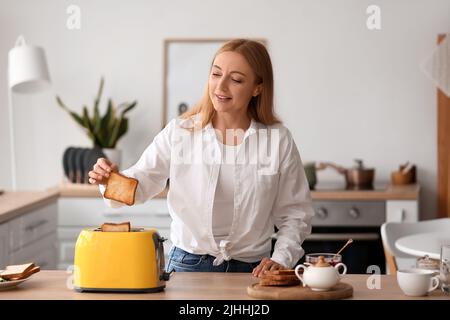 Mature woman making tasty toasts and drinking coffee in kitchen Stock ...
