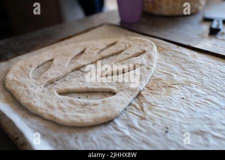 A baker shapes and cuts traditional French Fougasse bread. Front view ...