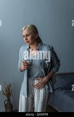 Menopause. Woman with glass of water suffering from heat flash at ...