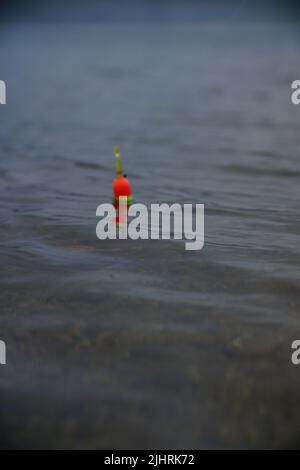 An orange and green fishing bobber floating in the water Stock Photo ...