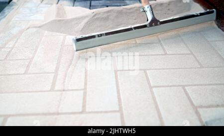 The principle of laying paving slabs. A worker spreads sand with a ...