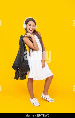 positive teen girl listen music in headphones on yellow background ...