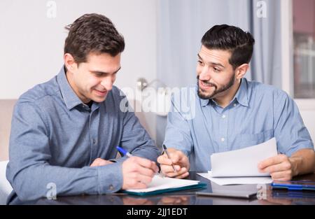 Two smiling friends discussing papers on couch Stock Photo - Alamy