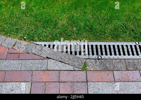 drainage grate bolted to storm drain at corner of pedestrian pavement ...