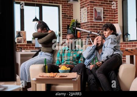 Group of scared friends gathering on sofa and watching horror movie ...