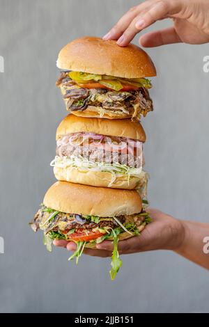 three homemade hamburgers with meat, cheese, lettuce, tomato on a Board ...