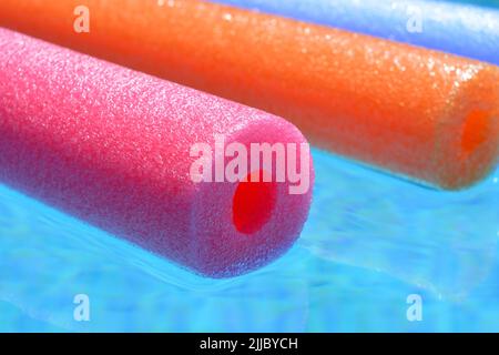 Pink pool noodle floating in a blue pool with refracted light on bottom ...