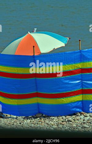 Red blue and yellow windbreaker with unbrella on beach at Sidmouth in ...