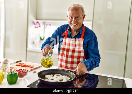 Senior man smiling confident pouring salt on frying pan at kitchen ...