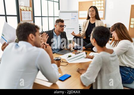 Businesswoman enjoys meditating during meeting. Sitting on desk near ...