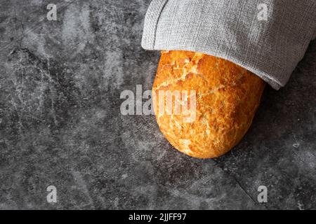 Tiger loaf of bread wrapped in a grey tea towel. On a black stone ...