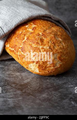 Tiger loaf of bread wrapped in a grey tea towel. On a black stone ...