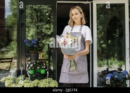 Attractive woman inviting to her flower shop. Beautiful smiling young ...