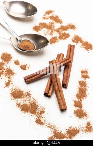 Cinnamon sticks among ground cinnamon, metal spoons on table. Close up ...