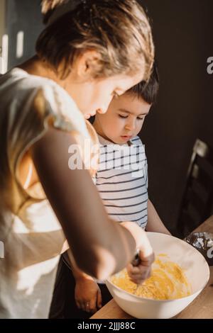 Son mixing ingredient with mother in kitchen at home Stock Photo - Alamy