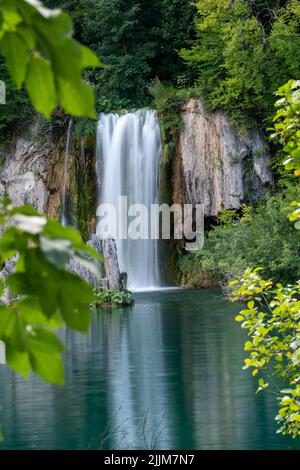 A vertical shot of a beautiful waterfall surrounded by rocks and green ...