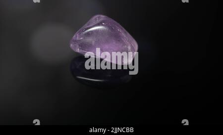 A polished pastel purple amethyst stone on a reflective black surface ...