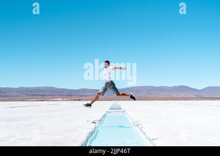 A closeup of a man jumping over a water in Salinas Grandes, Argentina ...