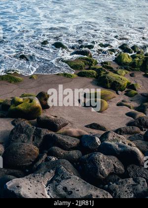 Closeup shot of rocks in the wavy sea under a sunset sky Stock Photo ...