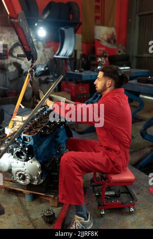 A vertical shot of a young Caucasian mechanic mounting the car engine ...
