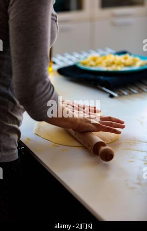 A vertical shot of a person rolling a dough with a rolling pin in the ...