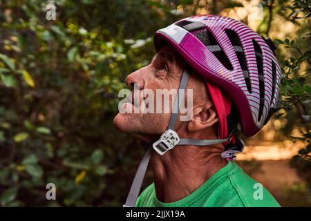 Closeup of senior male climber wearing safety helmet looking down while ...