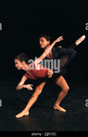 Full body danseur lifting ballerina while dancing on dark stage during ...