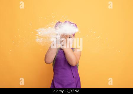 Optimistic girl in purple chef uniform clapping hands with white flour ...