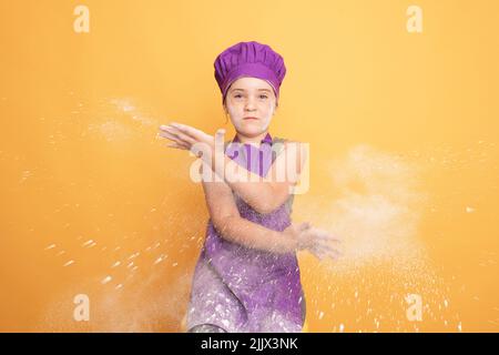 Optimistic girl in purple chef uniform clapping hands with white flour ...