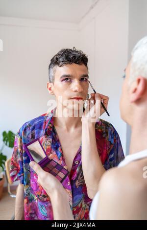 Caucasian transgender man getting makeup done by his boyfriend at home ...