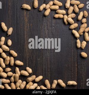 unpeeled peanuts in the peel scattered on a wooden table. space for ...