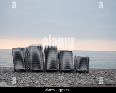Stacked plastic sun loungers on the beach. Sunbeds in bad weather ...