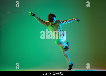 Energetic young man, fencer with smallsword practicing fencing isolated ...