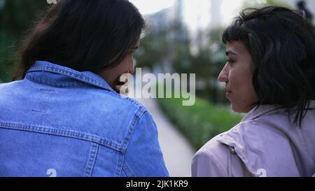 Female friends gossiping outside while walking together. Back of two ...