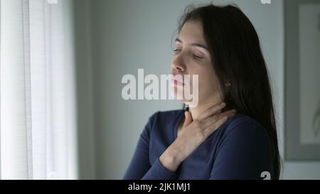 Anxious young woman trying to calm herself standing by window looking ...