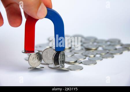 Hand holding magnet attracting silver coins with white cover background ...