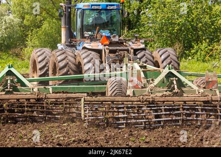 Blue tractor with double wheels pulling disc harrow with roller basket ...